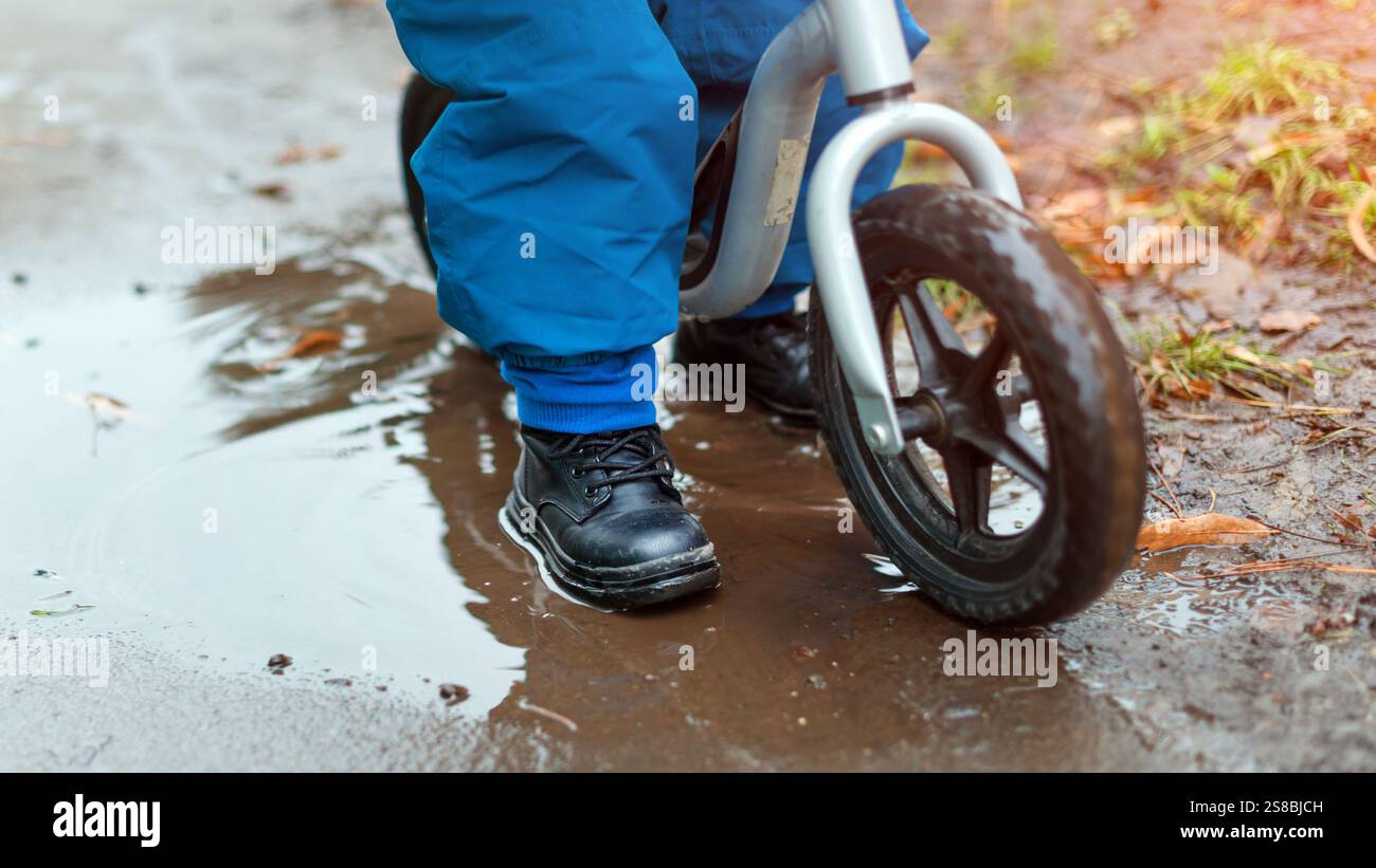 A child is riding a balance bike through a wet and muddy path with ...