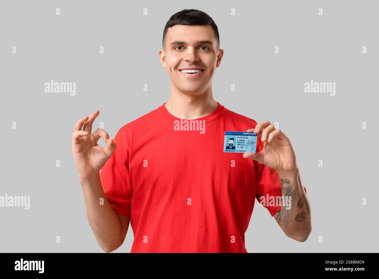 Young happy man holding driver license and showing OK gesture on grey ...