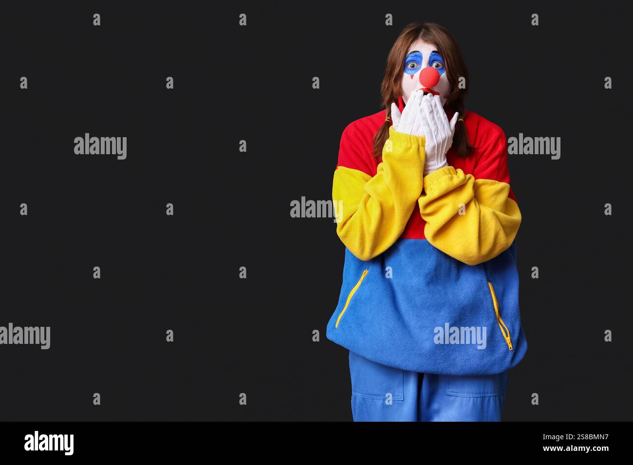 Young shocked woman dressed as sad clown on black background. April ...