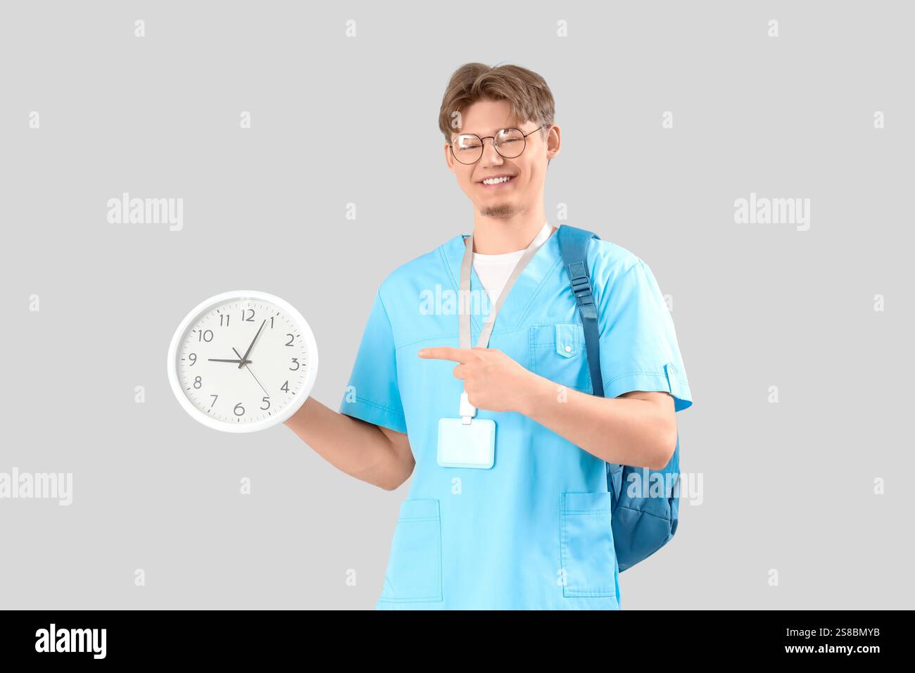 Male medical intern pointing at clock on light background Stock Photo ...