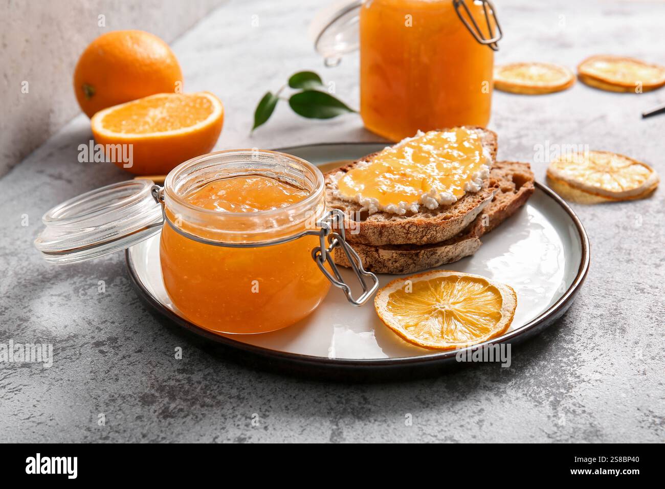 Plate with slices of bread and jar of sweet orange jam on grey ...