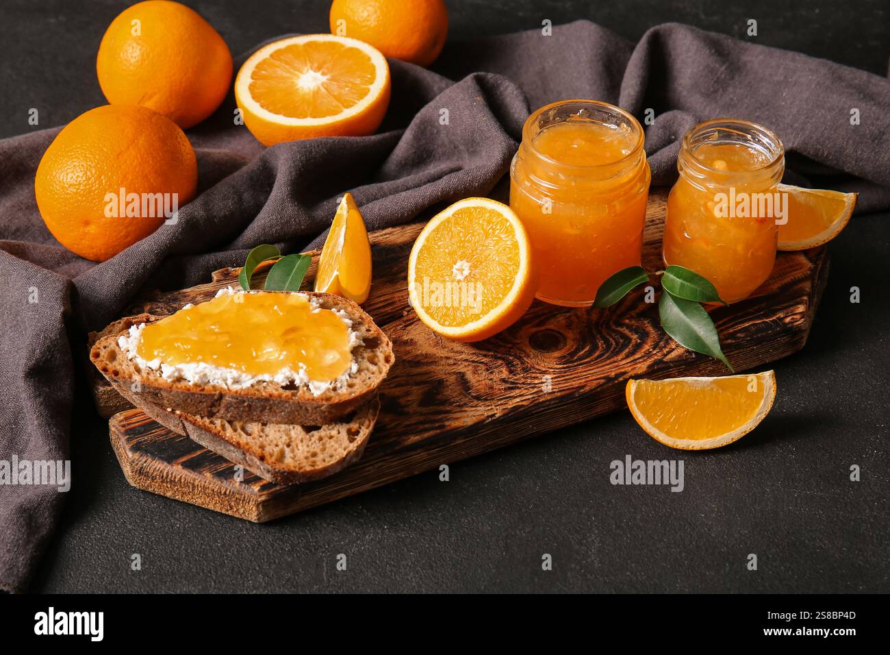 Wooden board with slices of bread and jars of sweet orange jam on black ...