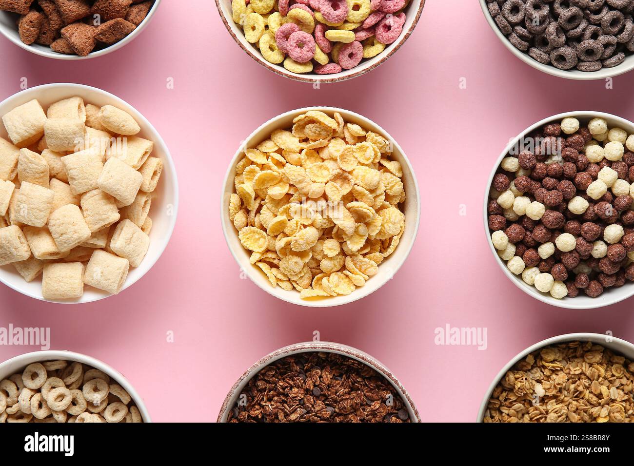 Bowls with different cornflakes on pink background Stock Photo - Alamy