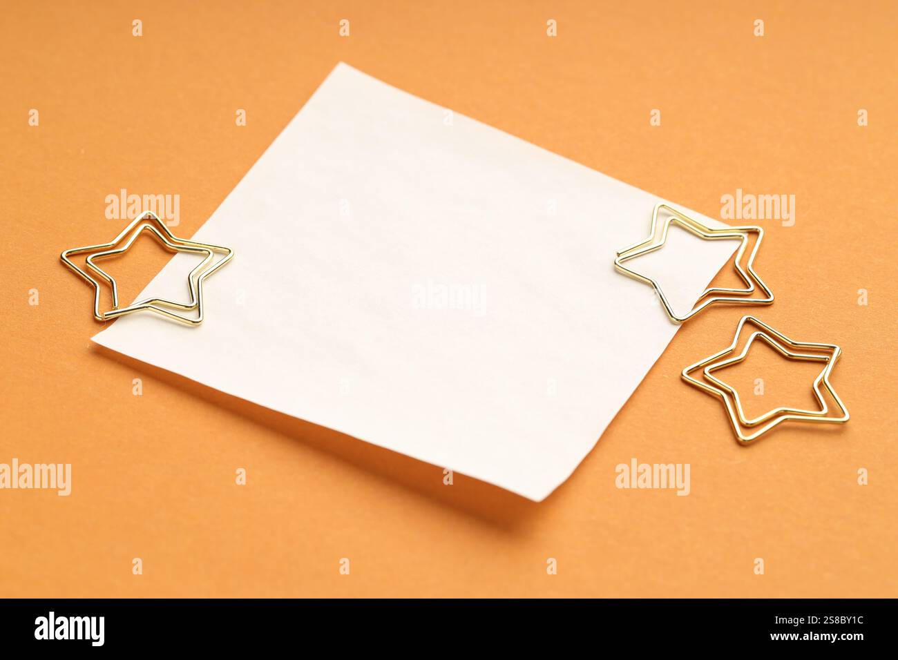 Star shaped clips and blank paper note on orange background, closeup ...