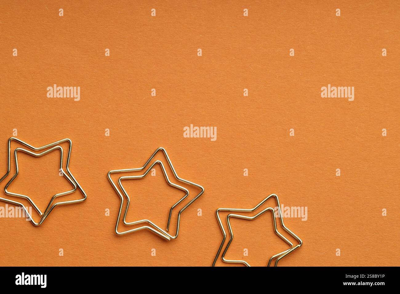 Star shaped paper clips on orange background, flat lay. Space for text ...