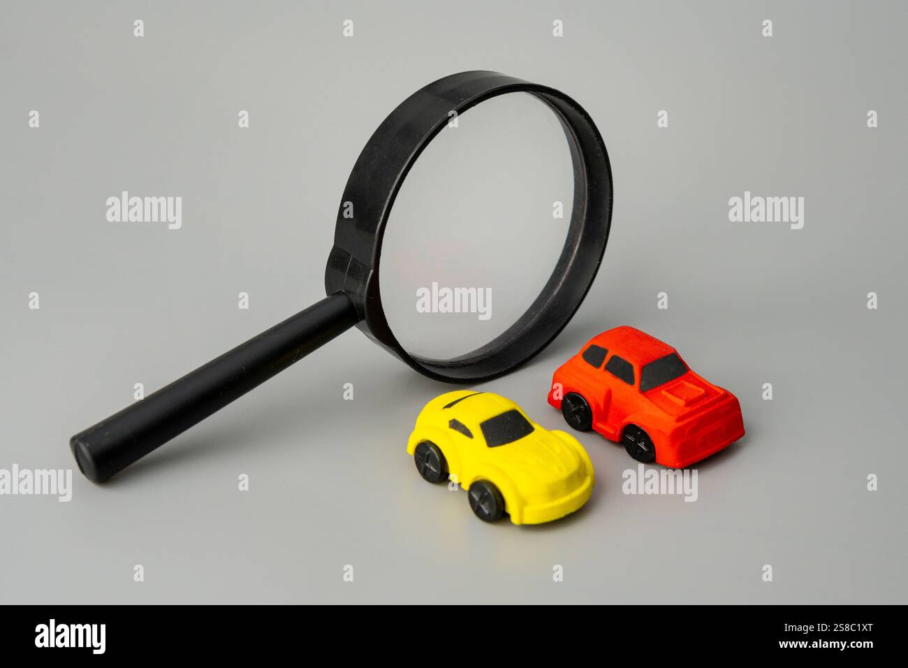 A magnifying glass and two toy cars. The process of comparing vehicles ...
