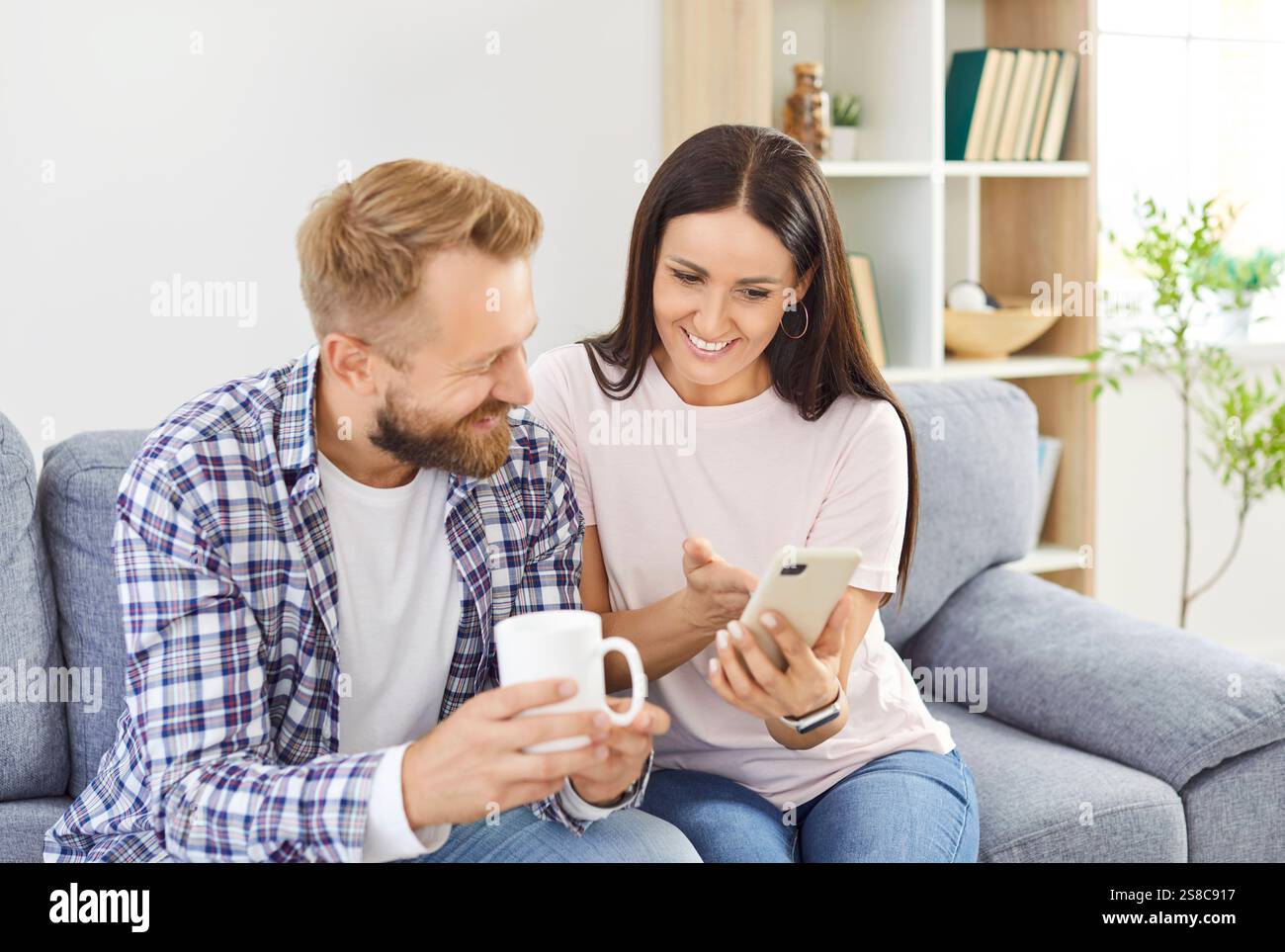 Young couple using mobile phone together sitting on sofa in living room ...