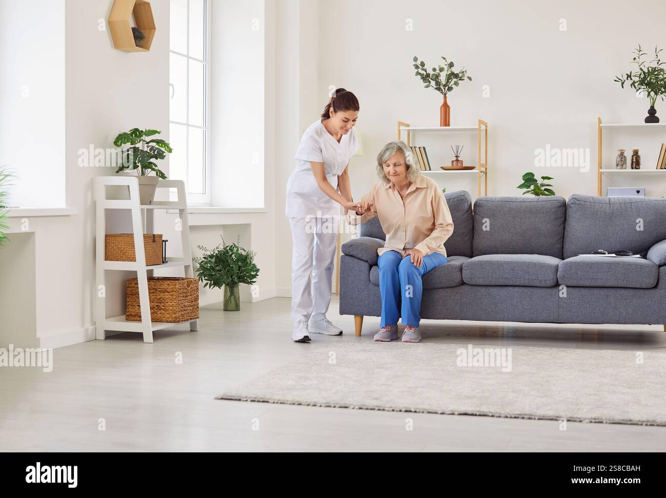 Caregiver helps a senior woman patient get up off the couch at the ...