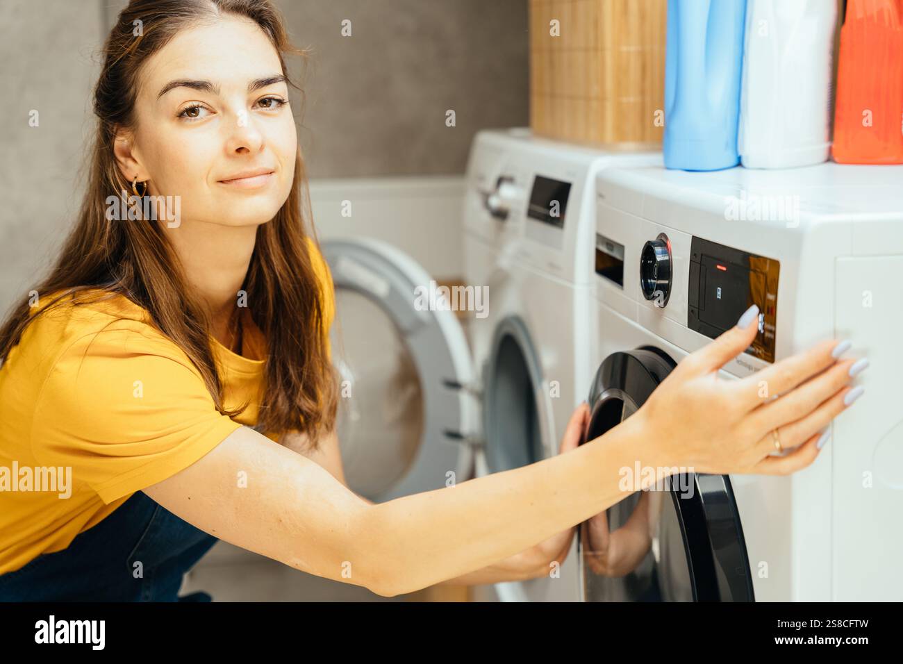 Beautiful young woman housewife doing housework, using washing machine ...