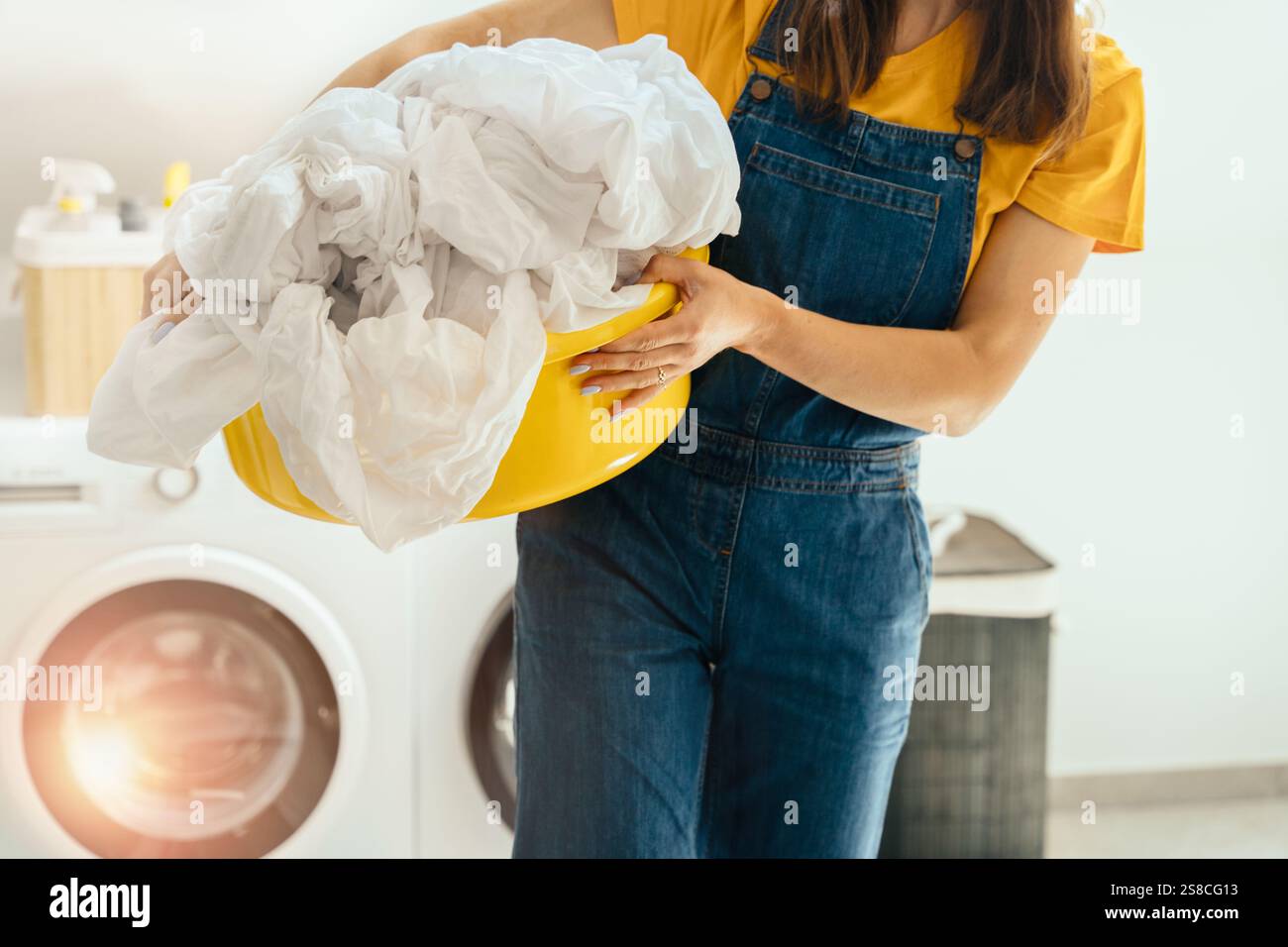 Portrait of lovely positive woman 30s holding a laundry basket with wet clothes in bathroom at ...