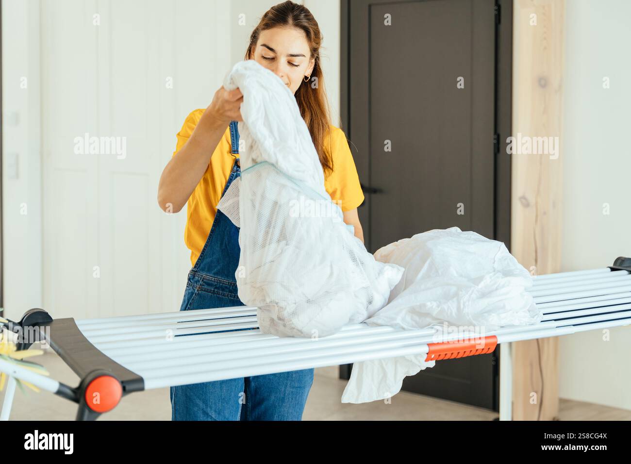 Beautiful young woman housewife wearing yellow t-shirt drying clothes ...