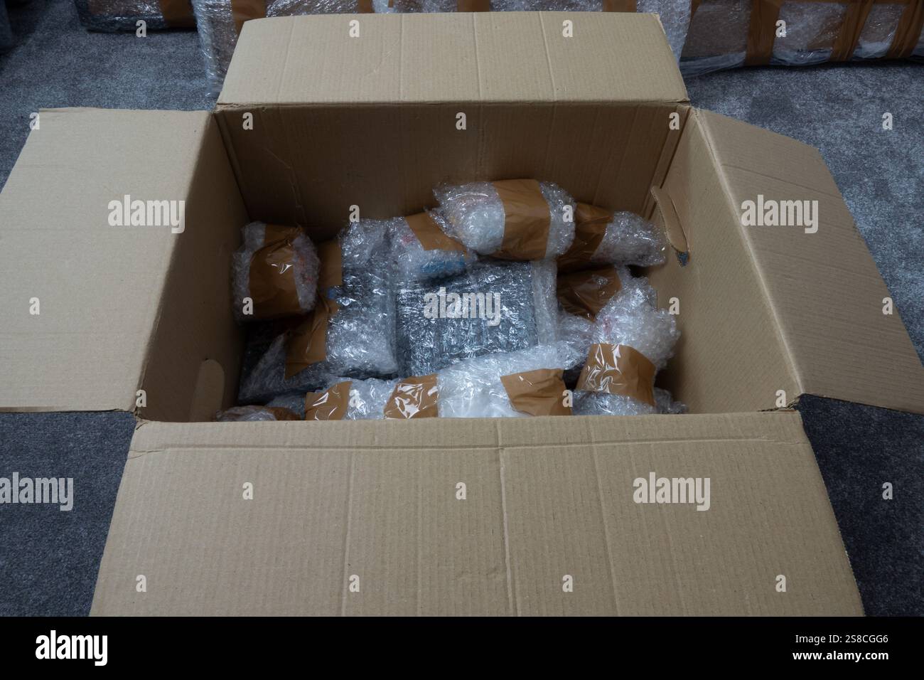 A cardboard box is filled with bubble-wrapped items. The box is open ...