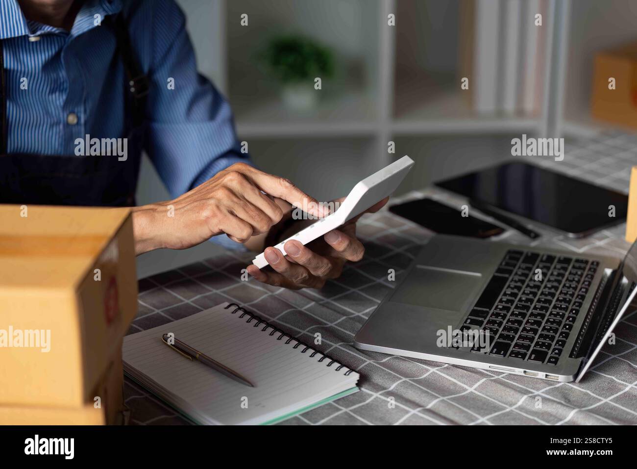 Online seller using a calculator on smartphone while checking inventory ...