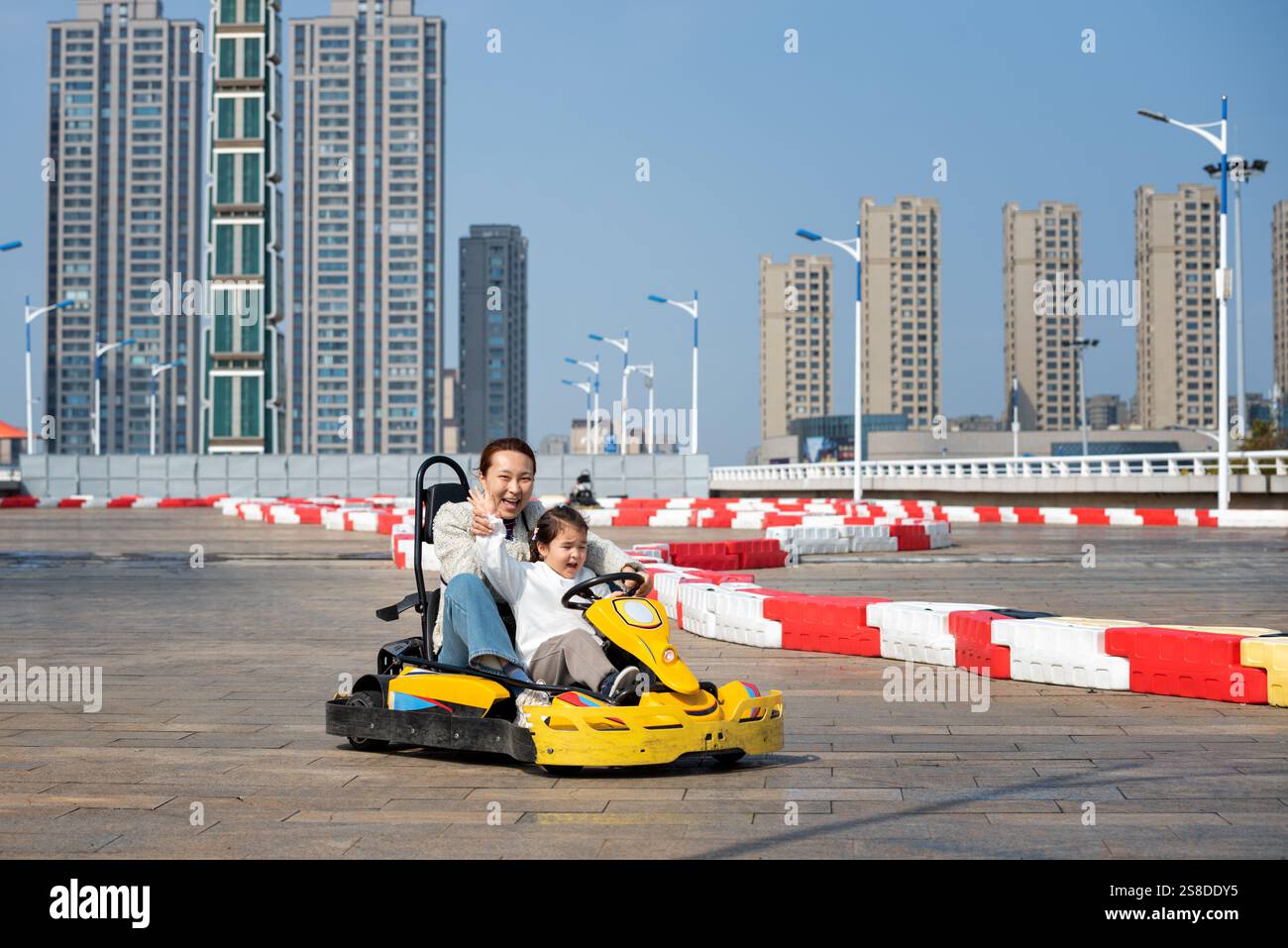 Mother driving kart with her daughter slowly at racing track outdoors ...