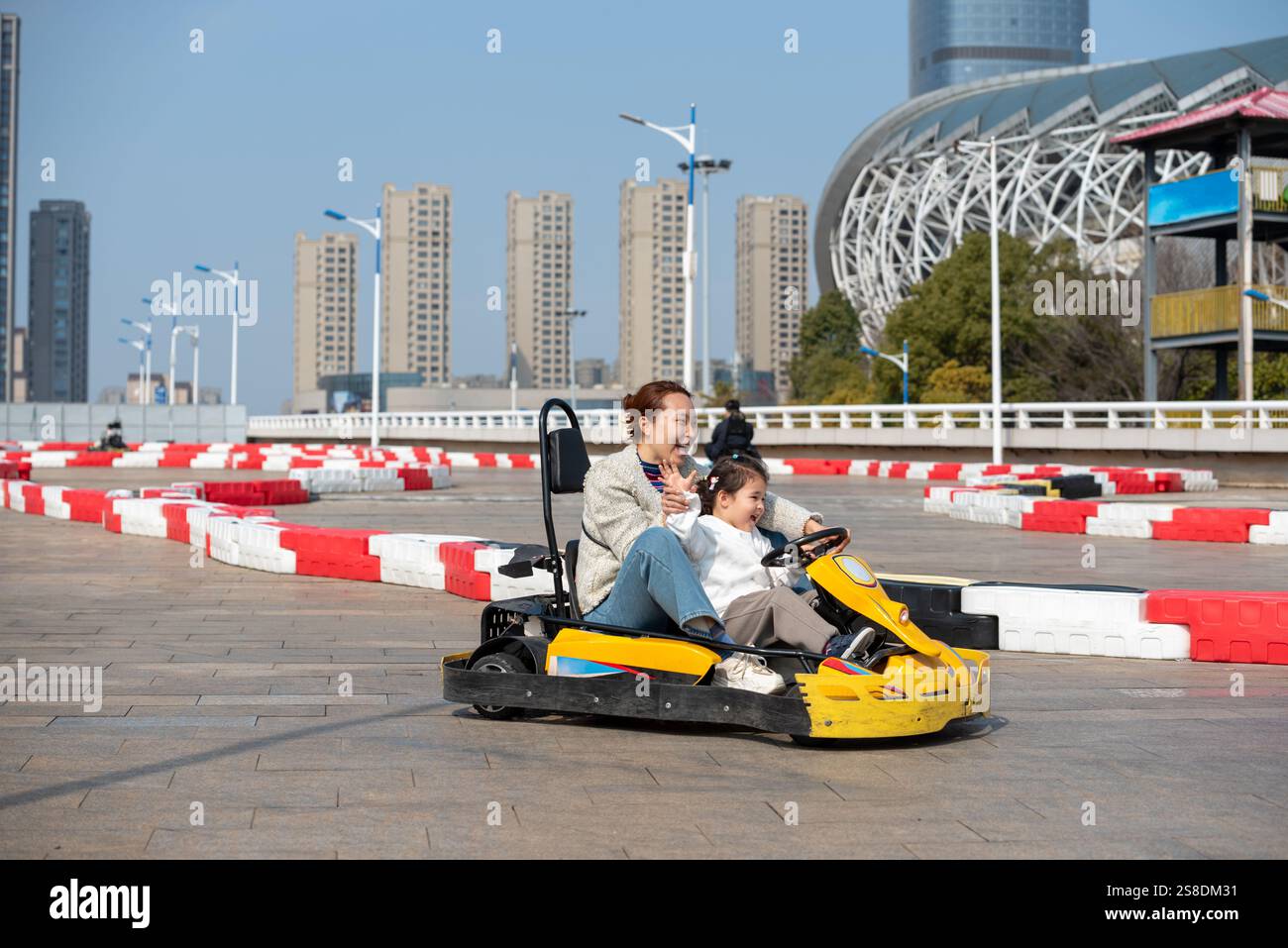 Mother driving kart with her daughter slowly at racing track outdoors ...