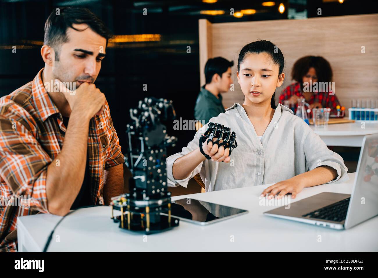 Teacher assists student constructing robotic arm in classroom for ...