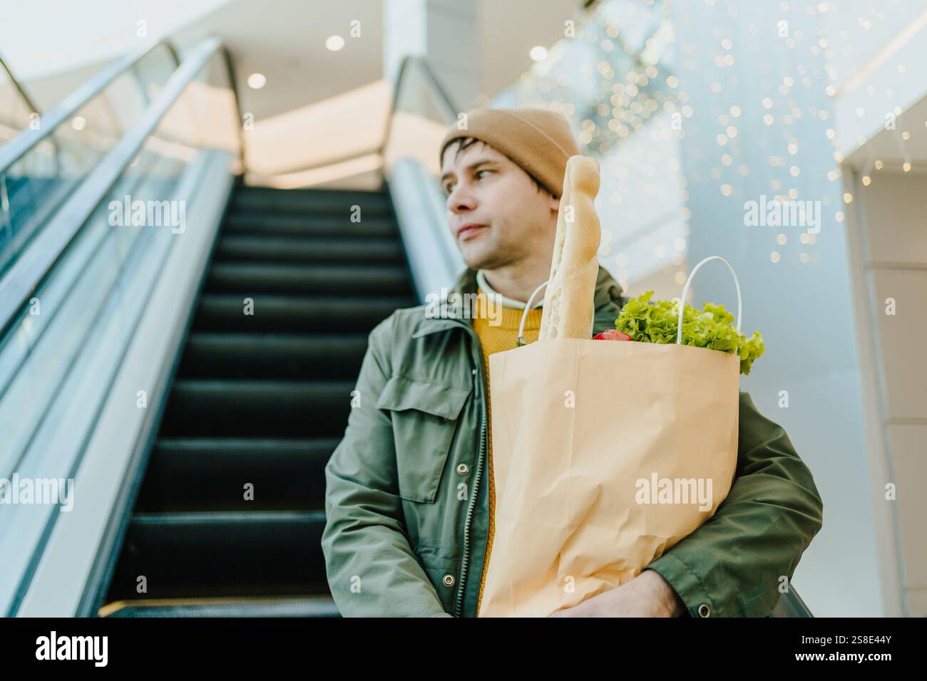 Conscious shopper standing near escalator with grocery bag, reflecting ...