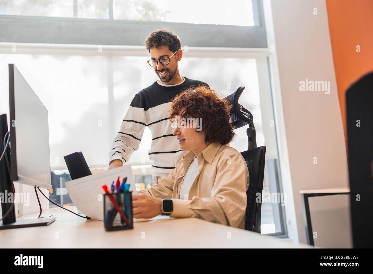 Two coworkers collaborate in a bright, modern office One sits, engaging ...