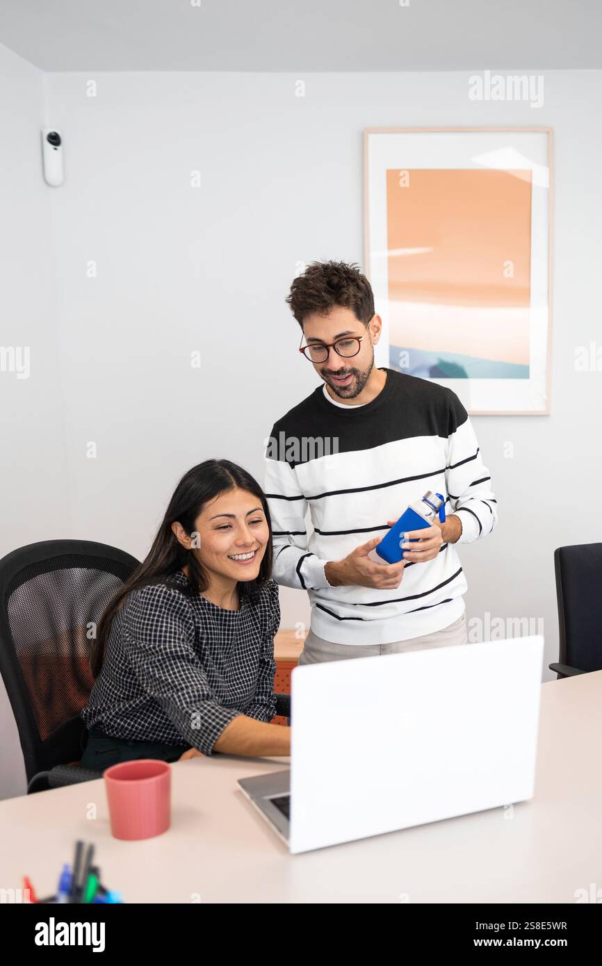 Two coworkers collaborate in an office setting, focused on a laptop ...