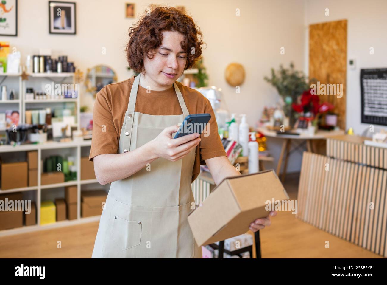 Retail store owner in an apron checks a package using their smartphone ...
