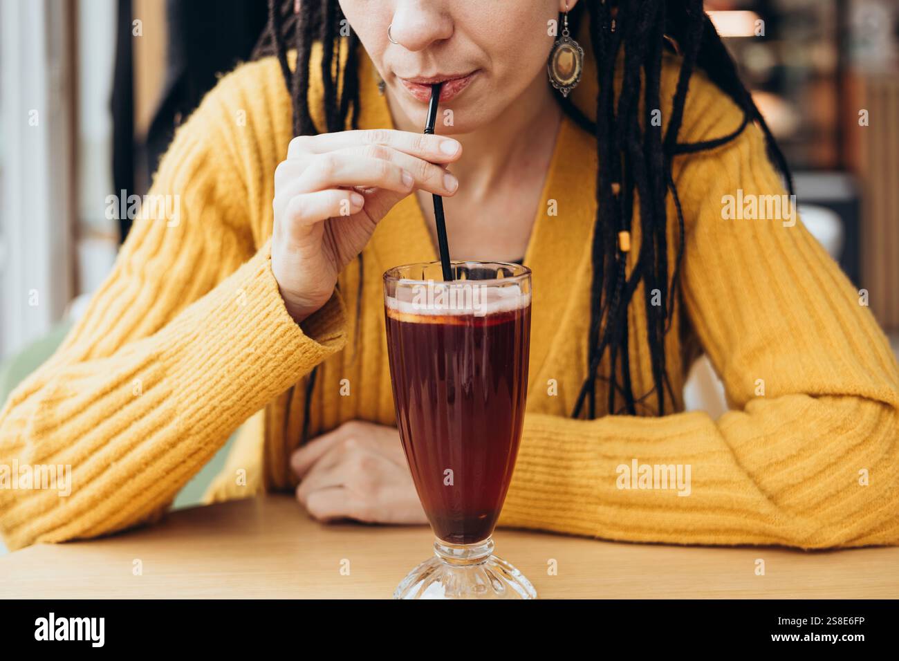 A woman in a yellow sweater sips a refreshing coffee drink through a ...