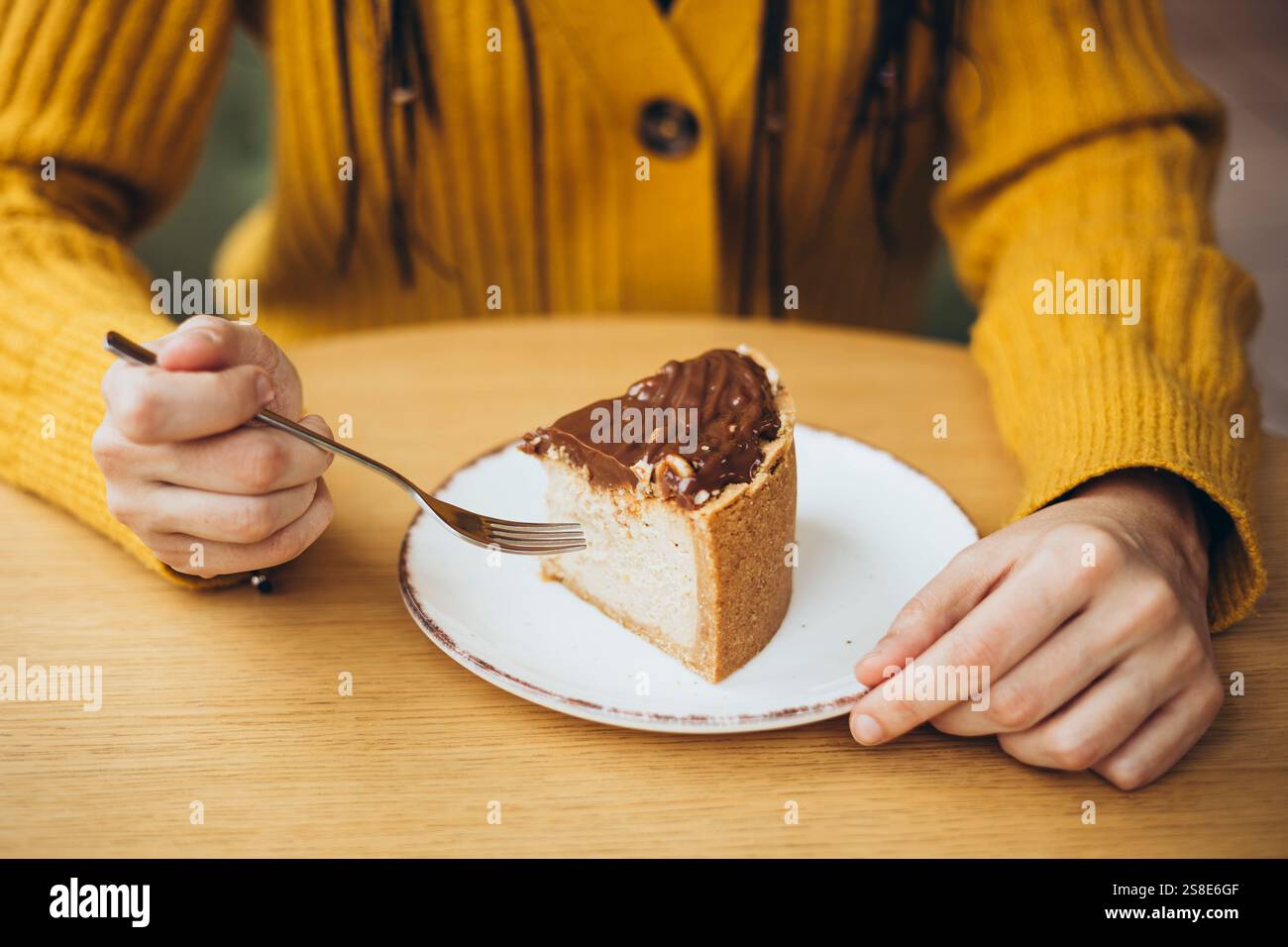 A person in a cozy yellow sweater enjoys a slice of chocolate-topped ...