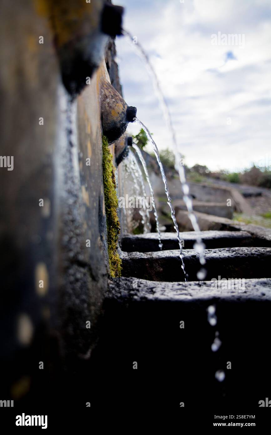 Close-up view captures water flowing through an old, moss-covered stone ...