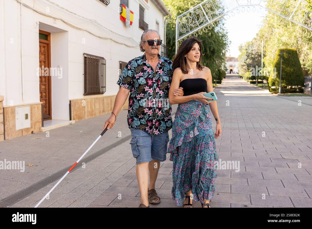 A blind father, utilizing a white cane, walks confidently through a ...