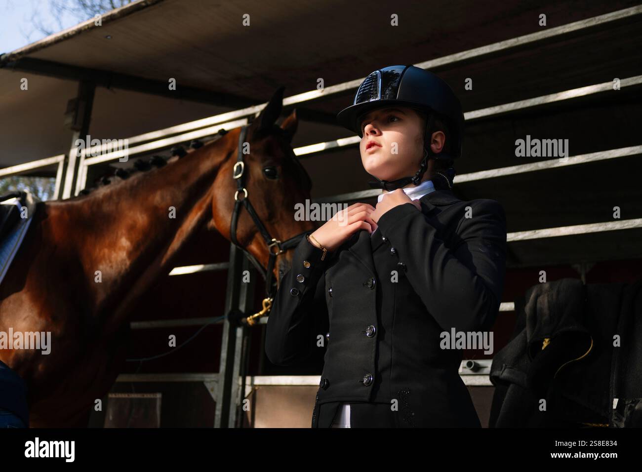 From below a teenage girl in classical dressage attire adjusts her ...