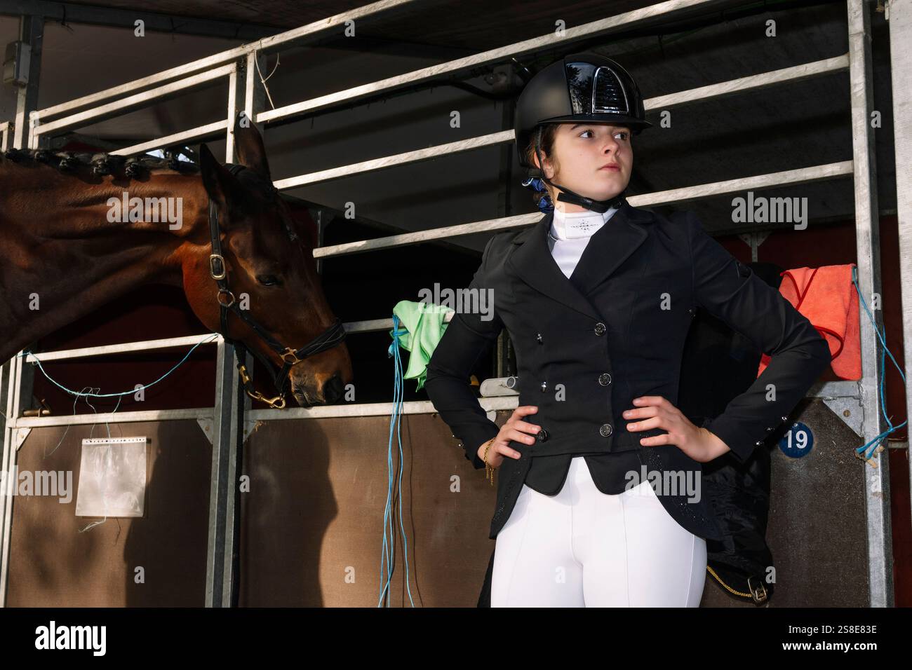 A teenage girl in traditional dressage attire stands confidently beside ...