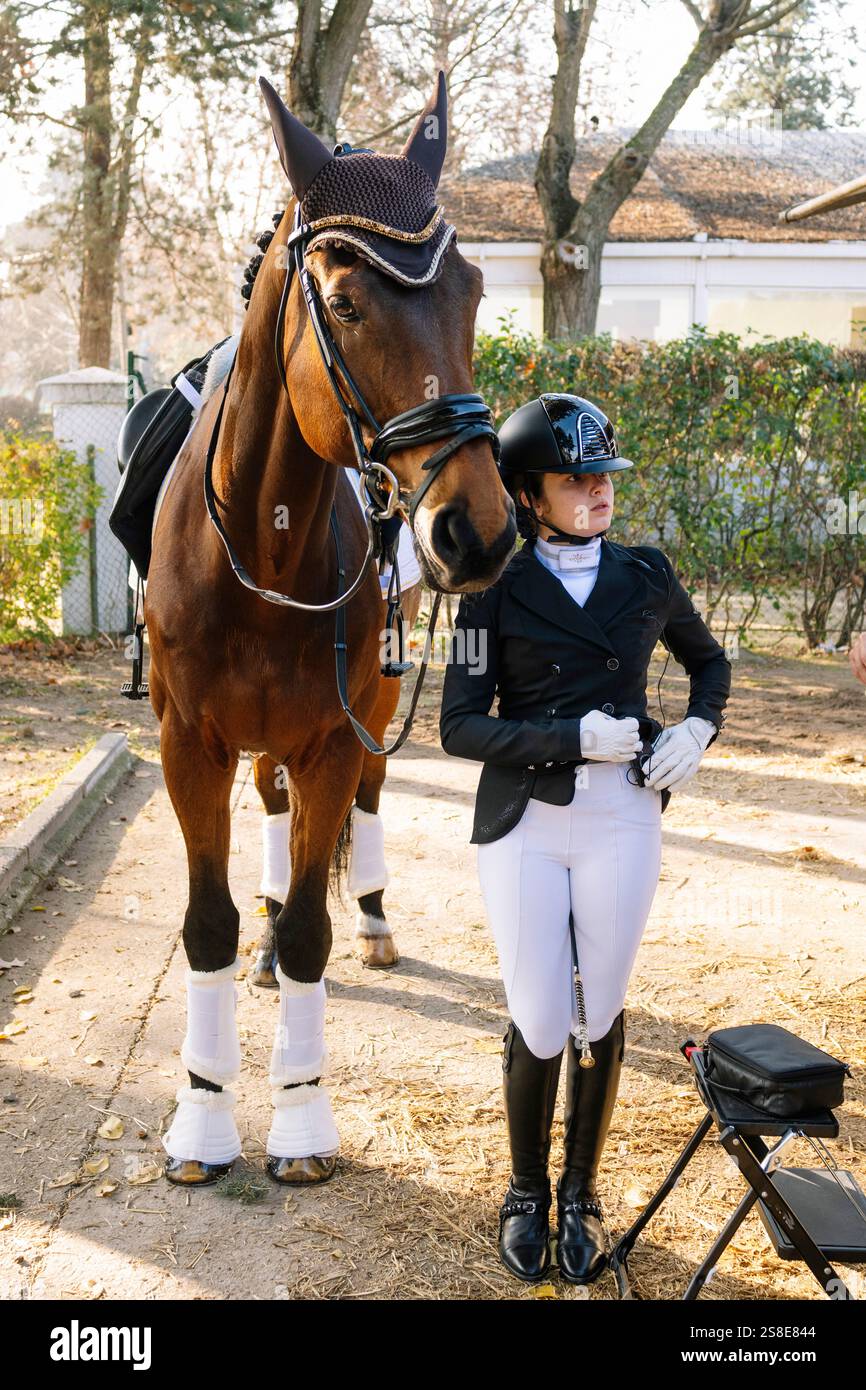 A teenage girl, dressed in traditional equestrian attire, stands beside ...