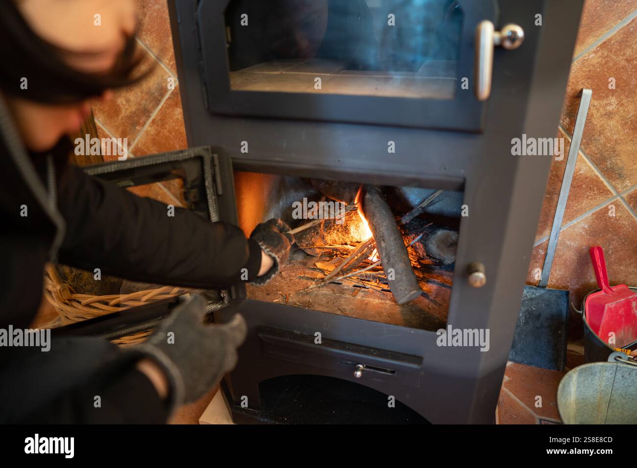 Cropped image of an Asian person wearing gloves as they stoke a wood ...