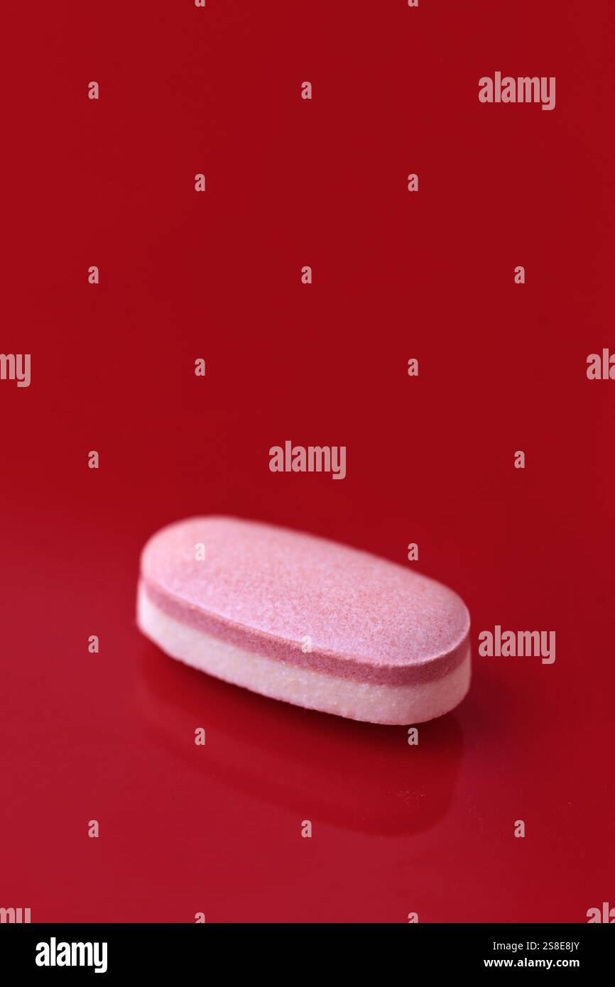 A single pink tablet placed centrally on a vivid red background ...
