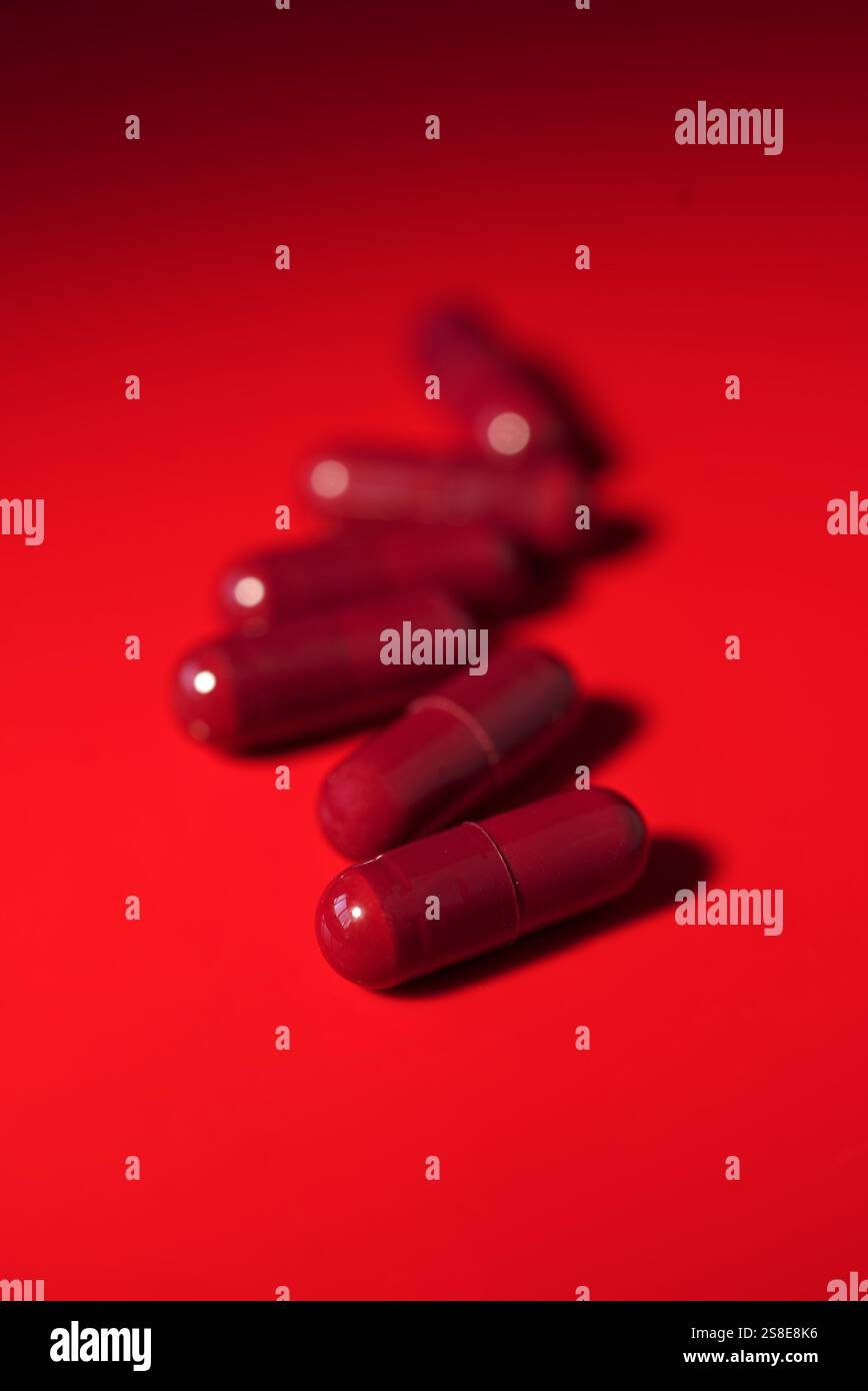 Vibrant image featuring red medical capsules scattered on a uniform red ...