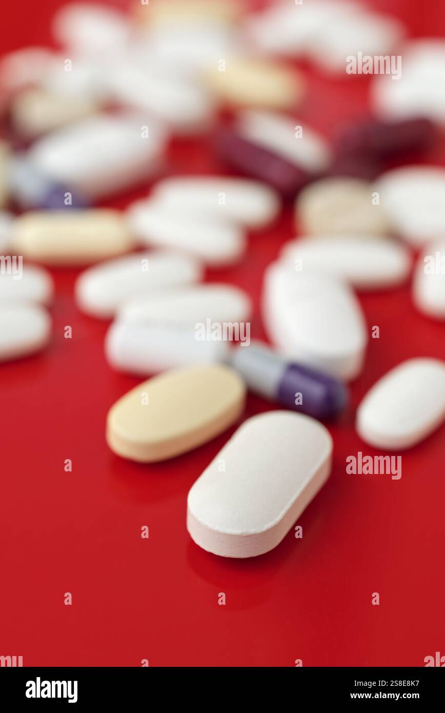A close-up image of various medical tablets scattered on a bright red ...