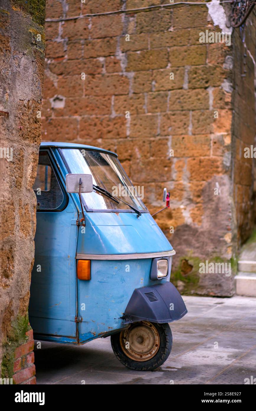 An iconic blue three-wheeled vehicle parked on a quiet, narrow street ...
