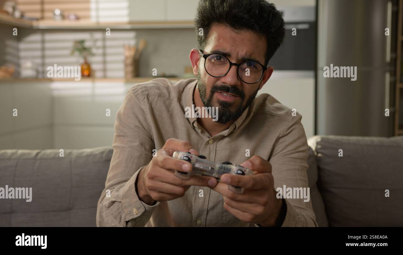 Arabian Indian man guy play video game at home kitchen on sofa male ...