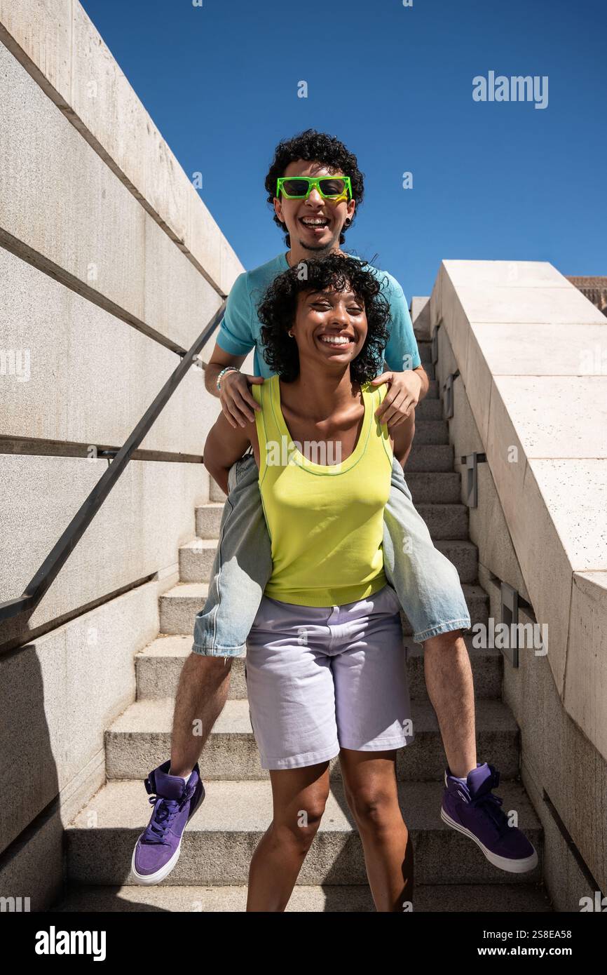 A cheerful multiethnic LGBTQ+ couple has fun outdoors, with one partner ...