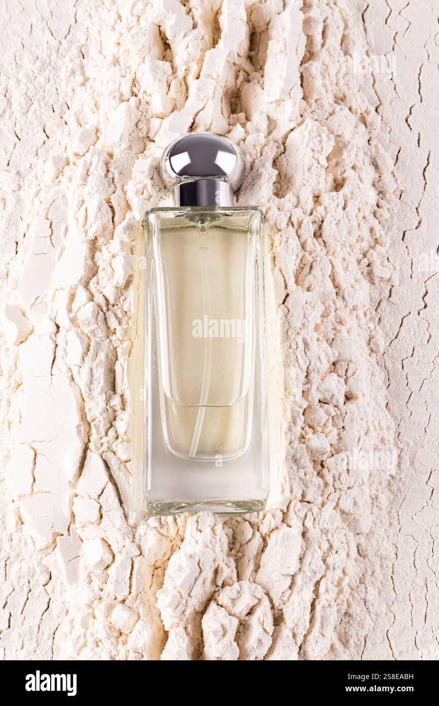 A sleek male perfume bottle rests on a cracked white sand texture ...