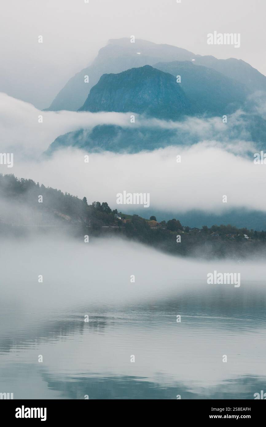 A peaceful lake reflects layers of mist and towering mountains in ...