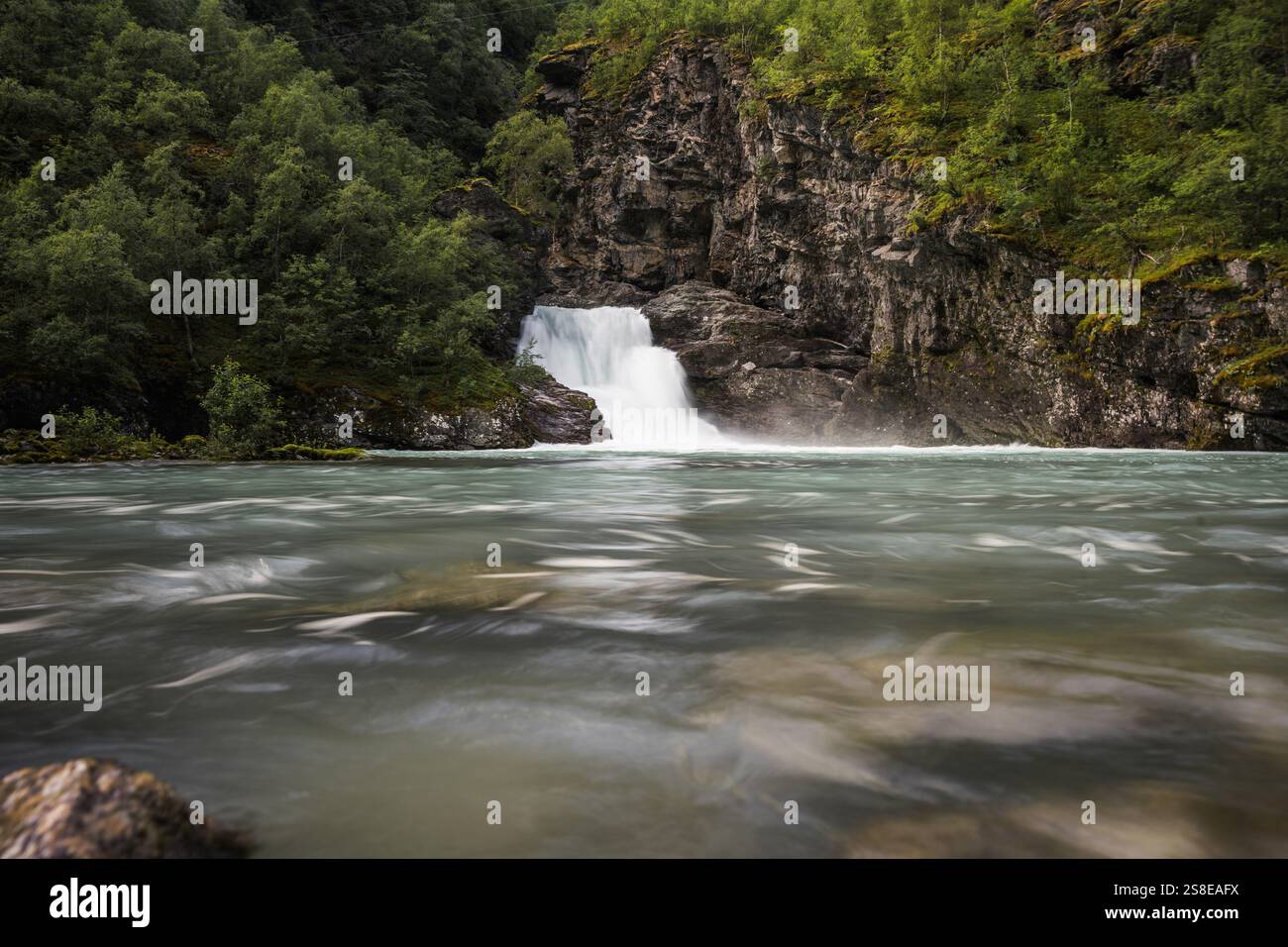 A peaceful waterfall cascades into a crystal-clear river surrounded by ...
