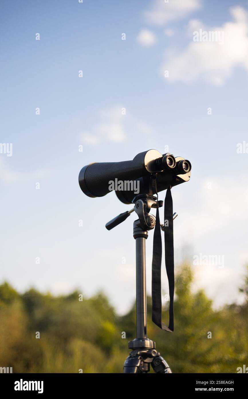 Black binoculars mounted on a tripod stand against a bright, clear blue ...