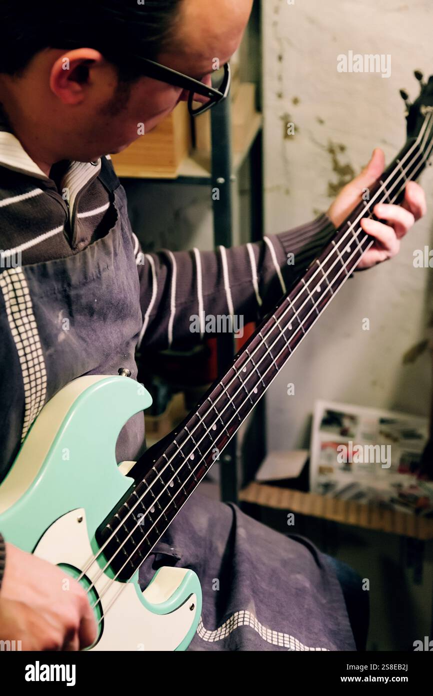 A skilled luthier works meticulously on a bass guitar in a workshop ...
