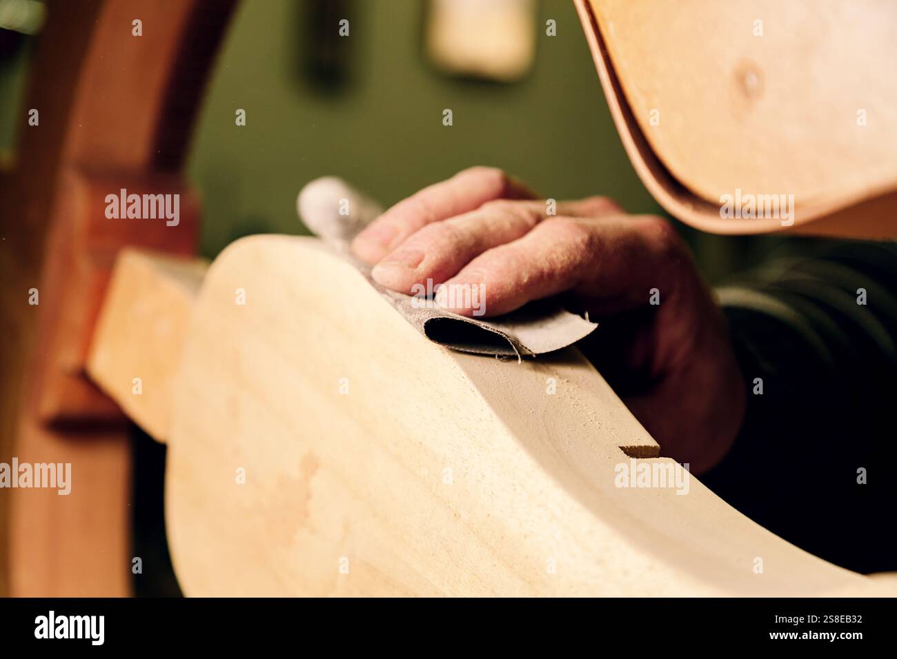 A luthier's hand meticulously shapes a bass guitar body using sandpaper ...