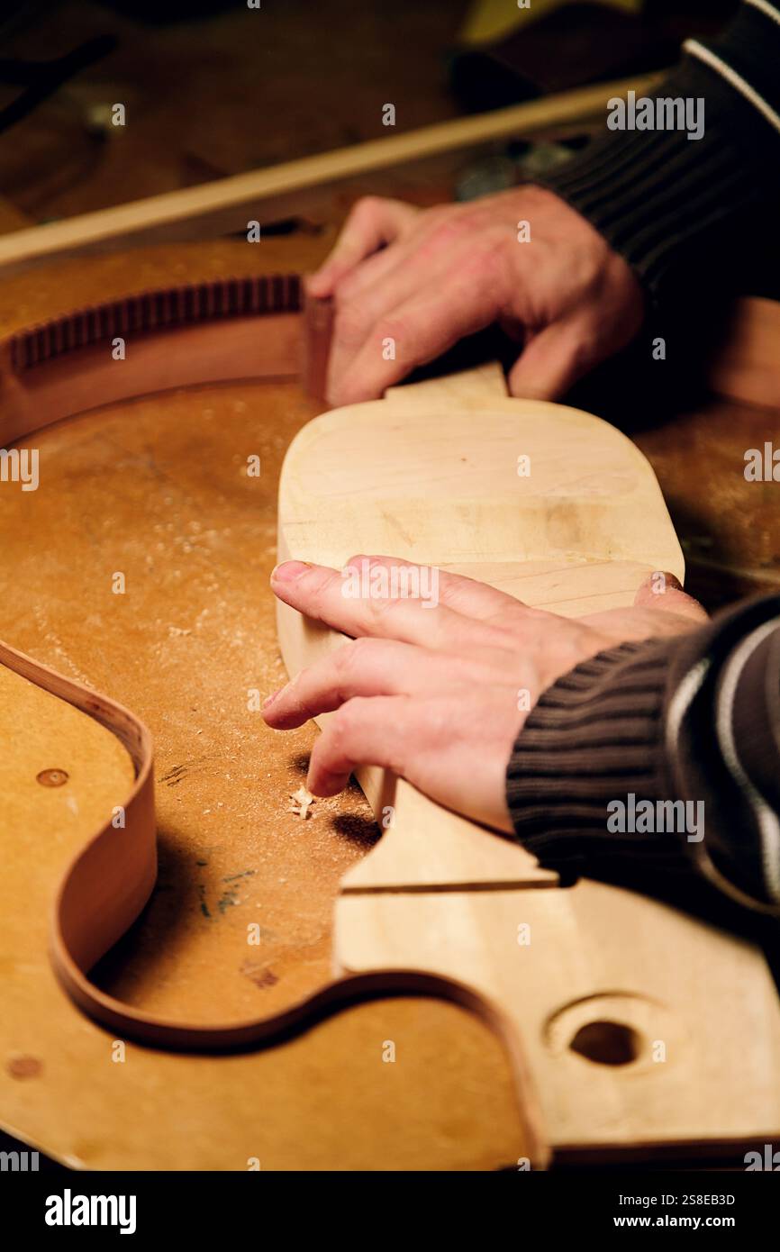 A skilled luthier shapes a bass guitar body, focusing on precision and ...