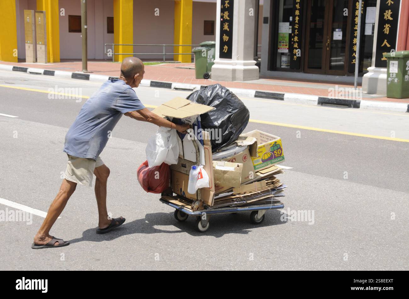An Asian street cleaner, ferrying a load of discarded cardboard on his ...
