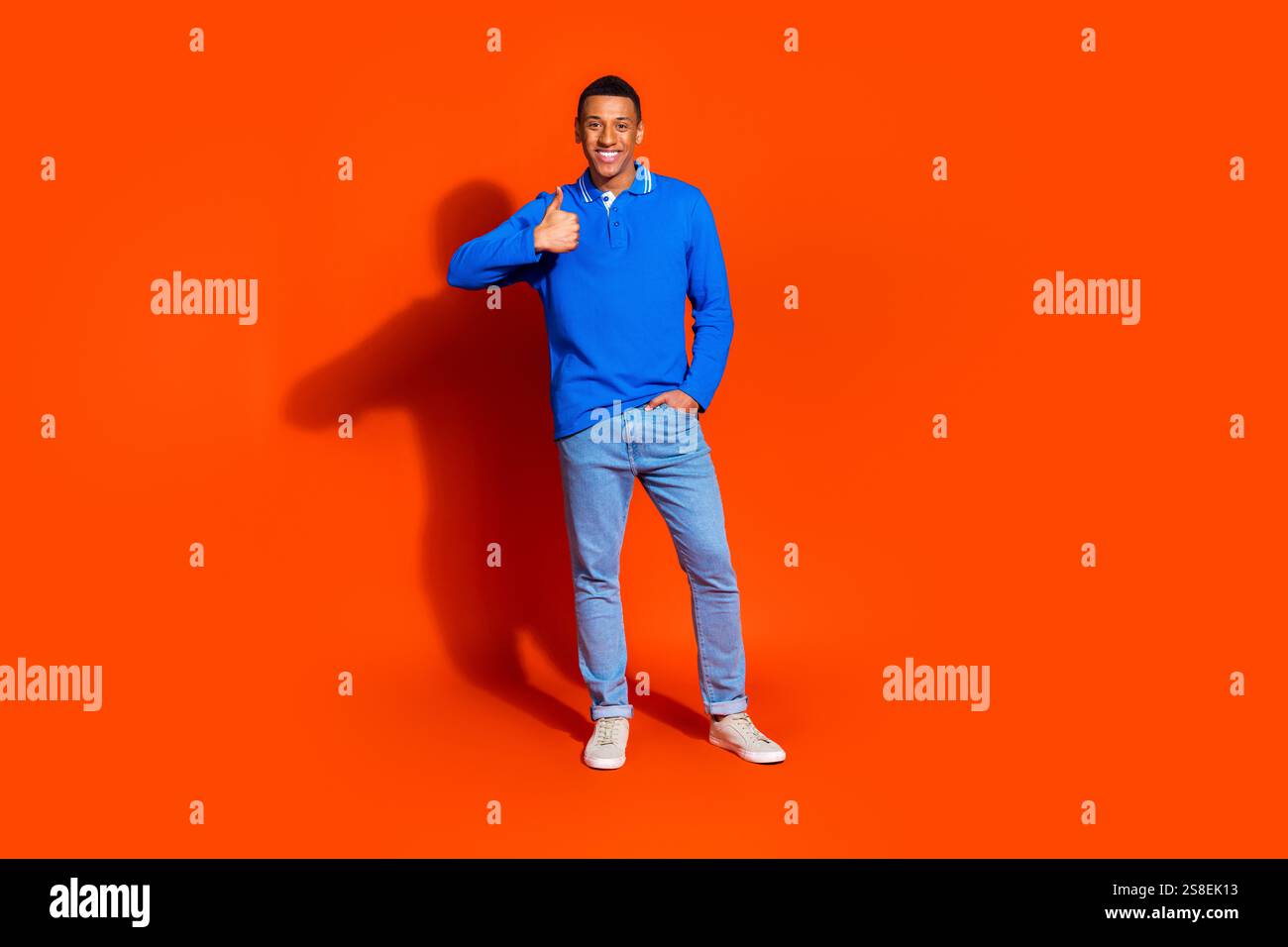 Young man in blue polo giving thumbs up against bright orange ...