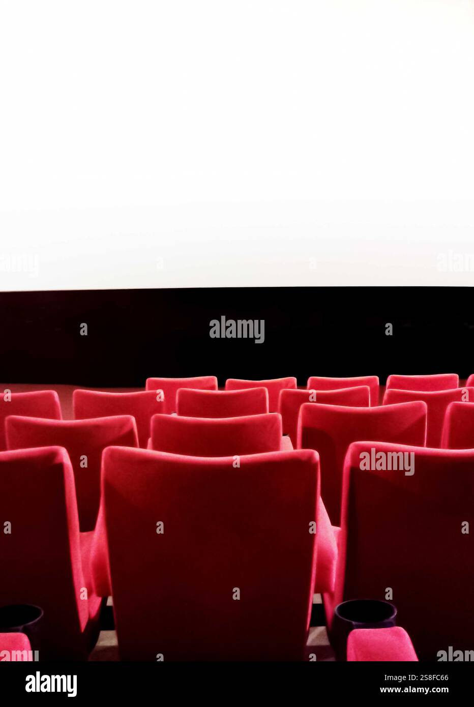 Rows of empty red seats are positioned in front of a large blank screen in a cinema. The setting ...