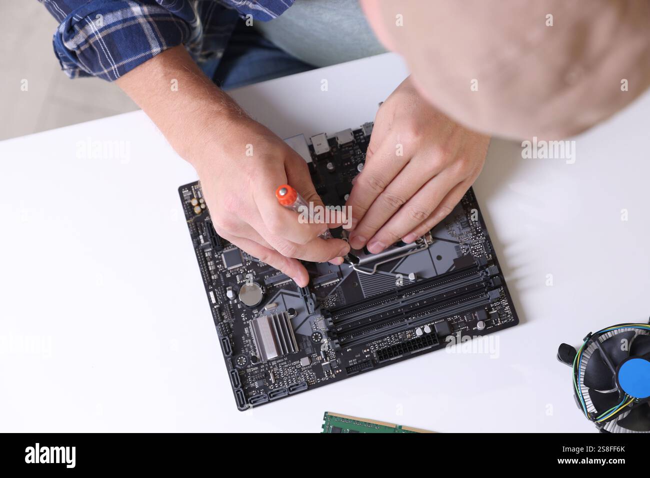 Man installing computer chip onto motherboard at white table, top view ...