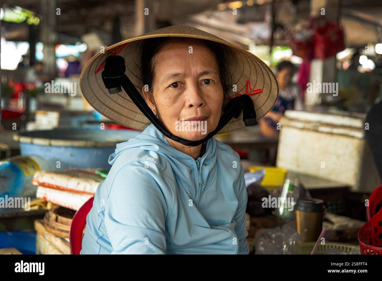 a thoughtful looking Vietnamese lady market trader sits at her stalll ...